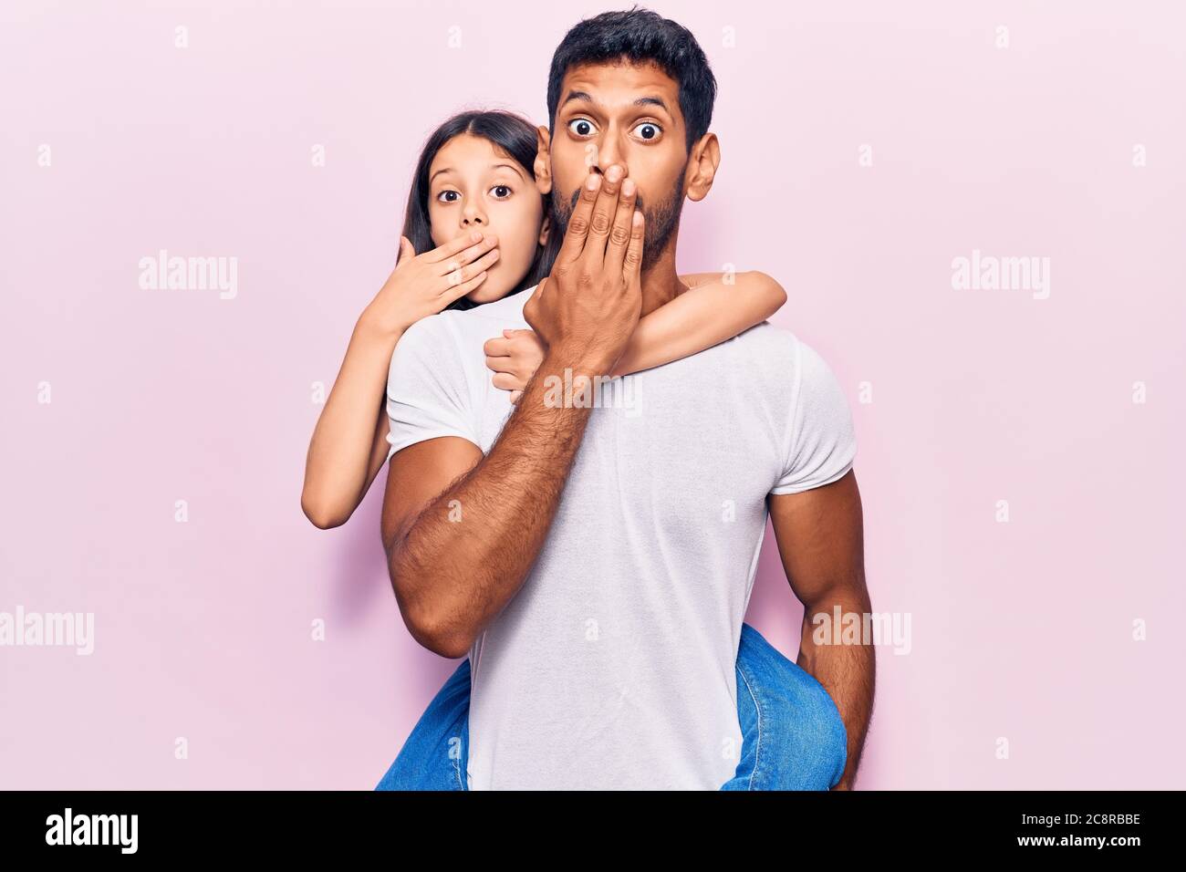 Latin father and daughter wearing casual clothes covering mouth with ...