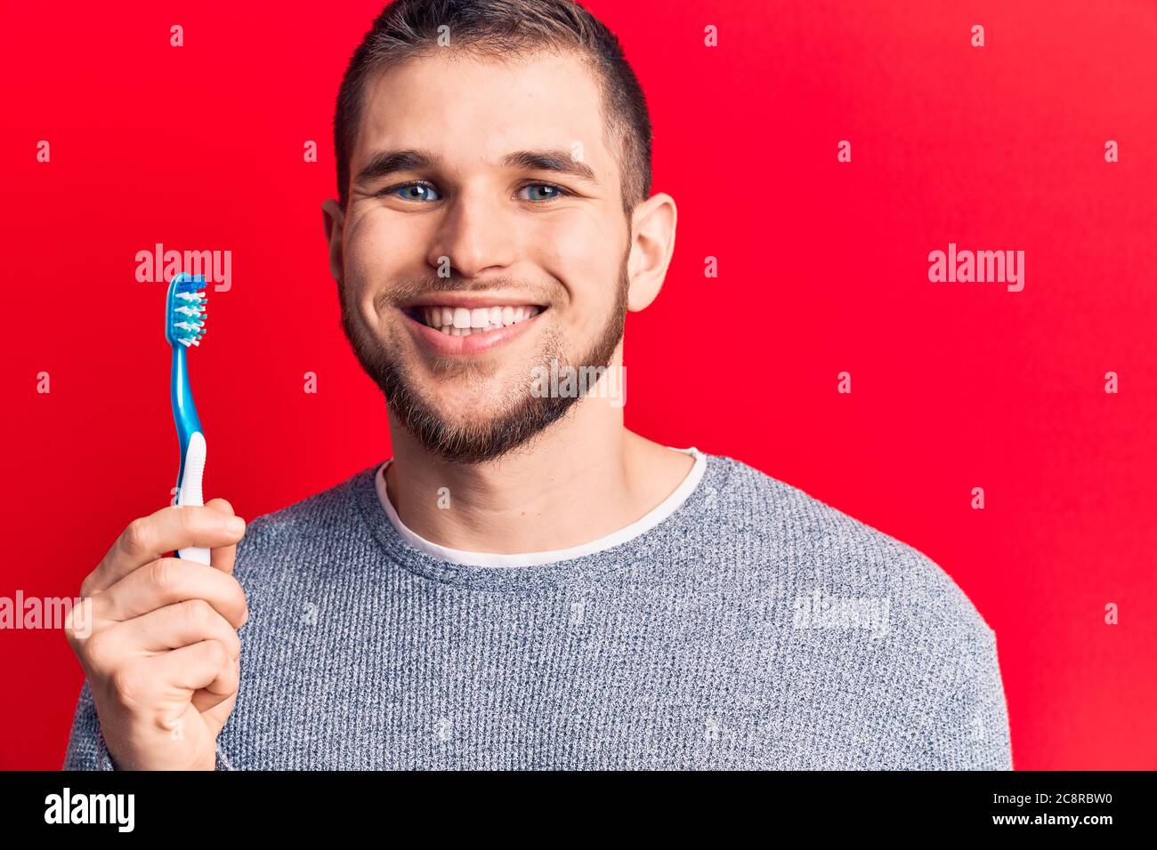 Young handsome man holding toothbrush looking positive and happy ...