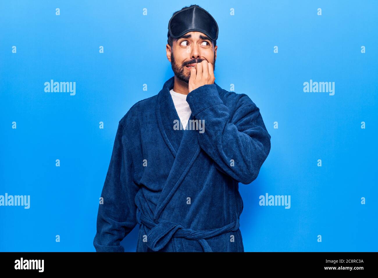 Young hispanic man wearing sleep mask and robe looking stressed and ...