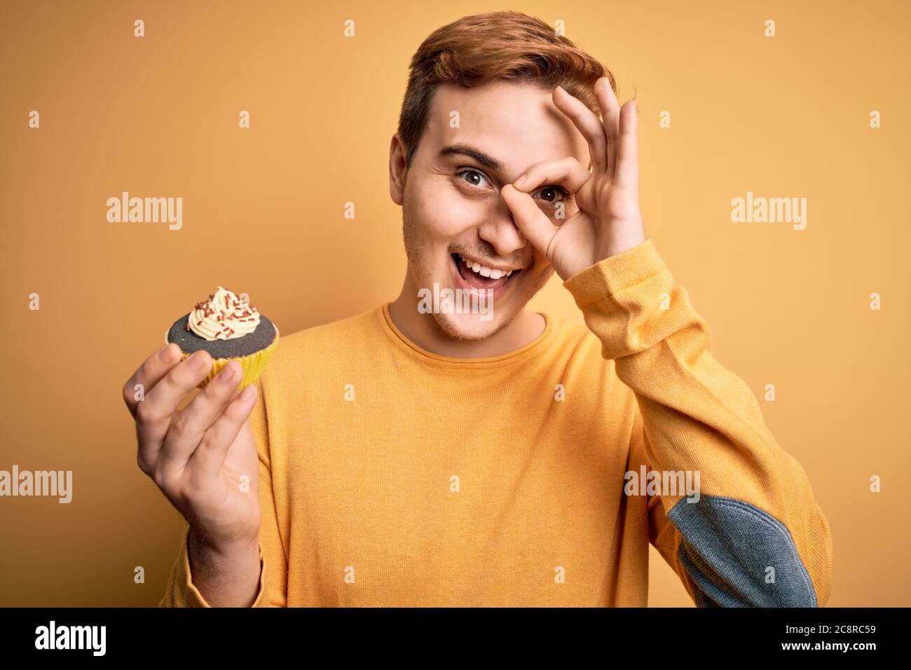 Young handsome redhead man eating sweet chocolate cupcake dessert over ...