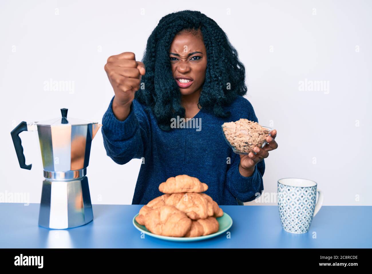 Beautiful african woman sitting on the table eating cereals annoyed and ...