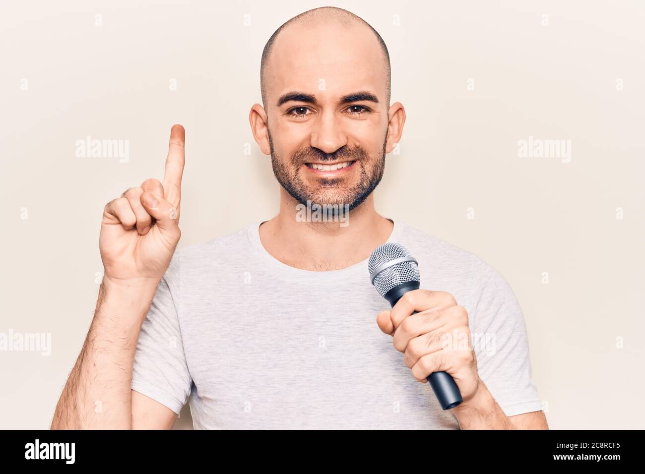 Young handsome bald man singing song using microphone smiling with an ...