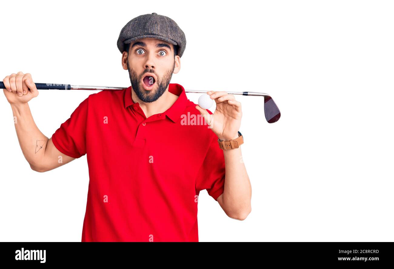 Young handsome man with beard playing golf holding club and ball scared ...