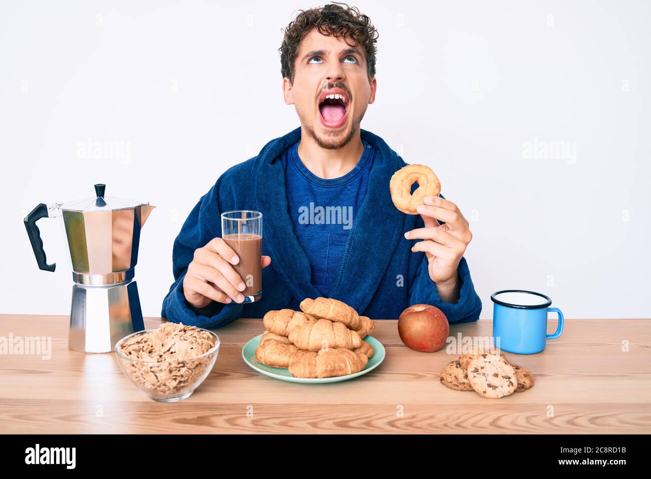 Young caucasian man with curly hair eating breakfast holding chocolate ...
