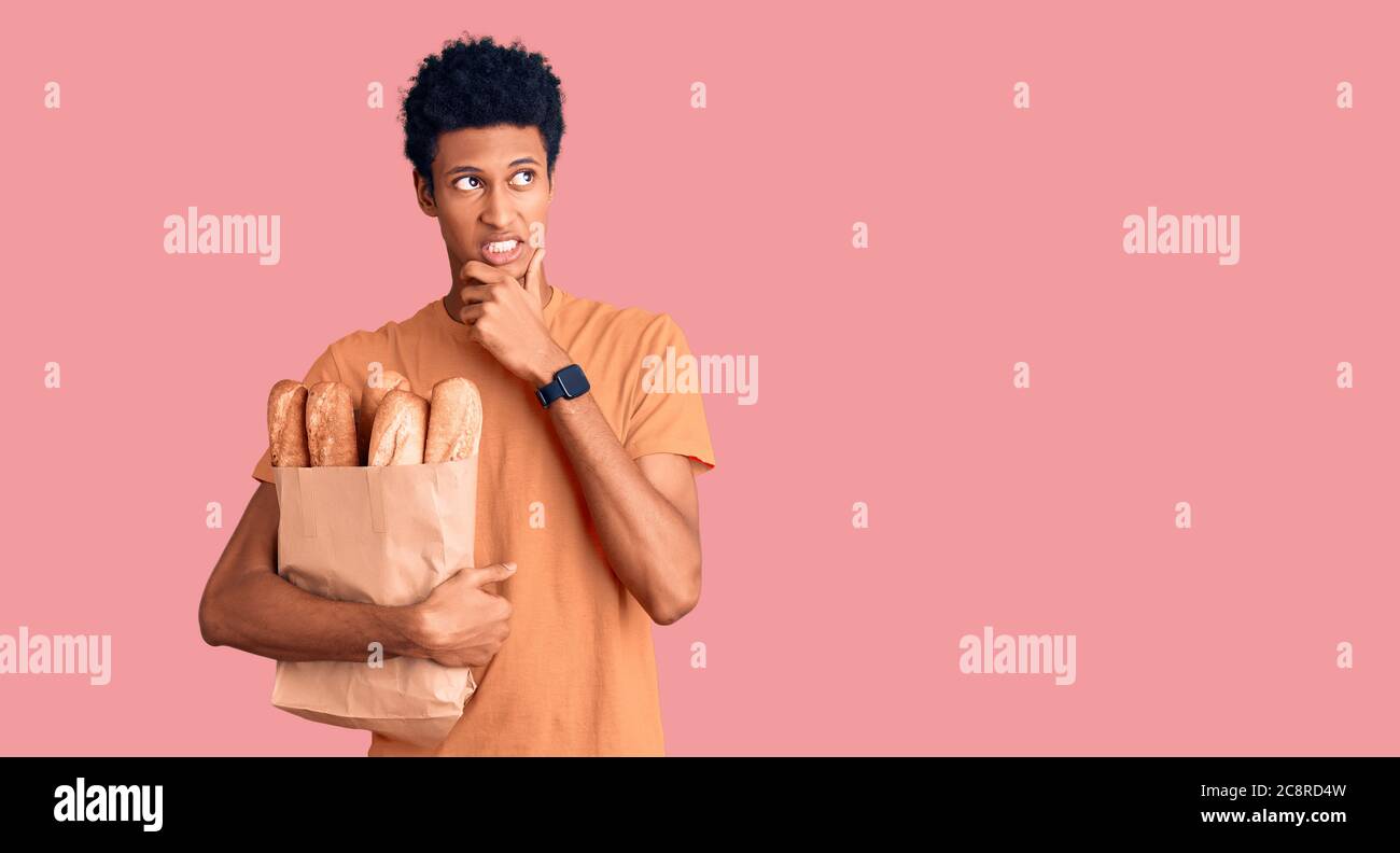 Young african american man holding paper bag with bread thinking ...