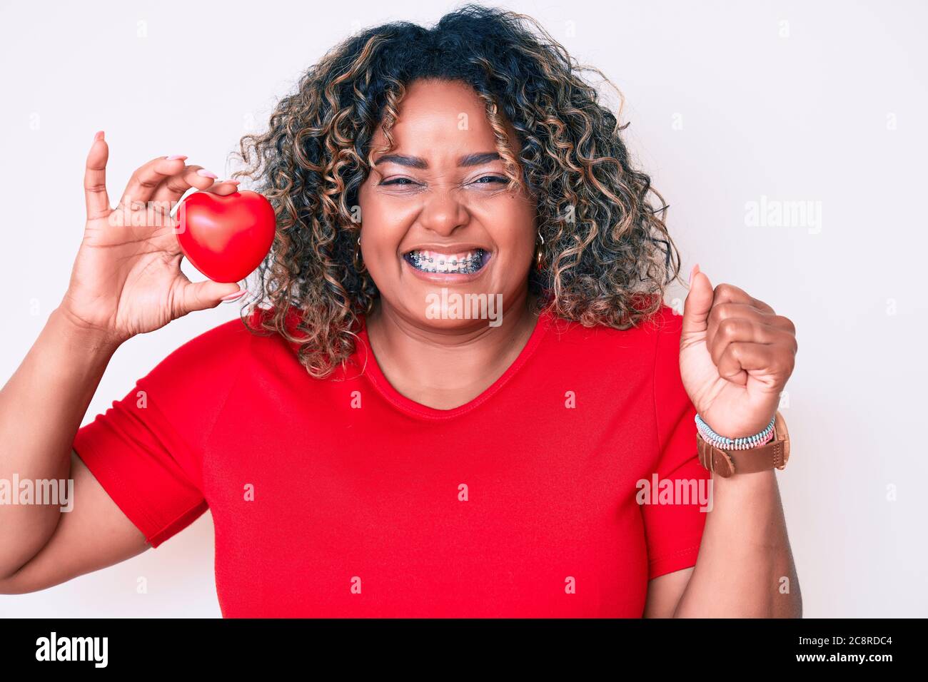 Young african american plus size woman holding heart screaming proud ...
