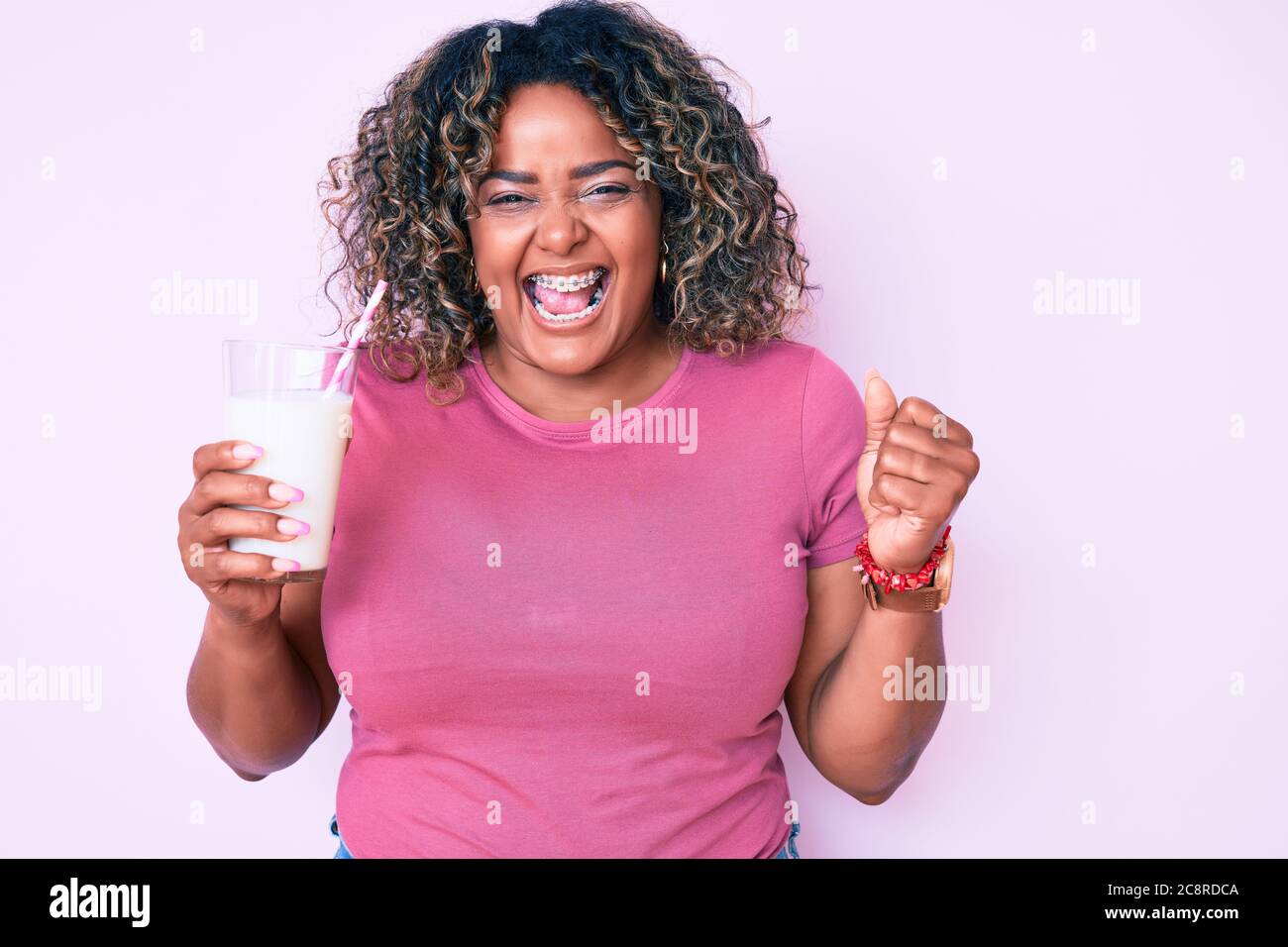Young african american plus size woman drinking glass of milk screaming ...