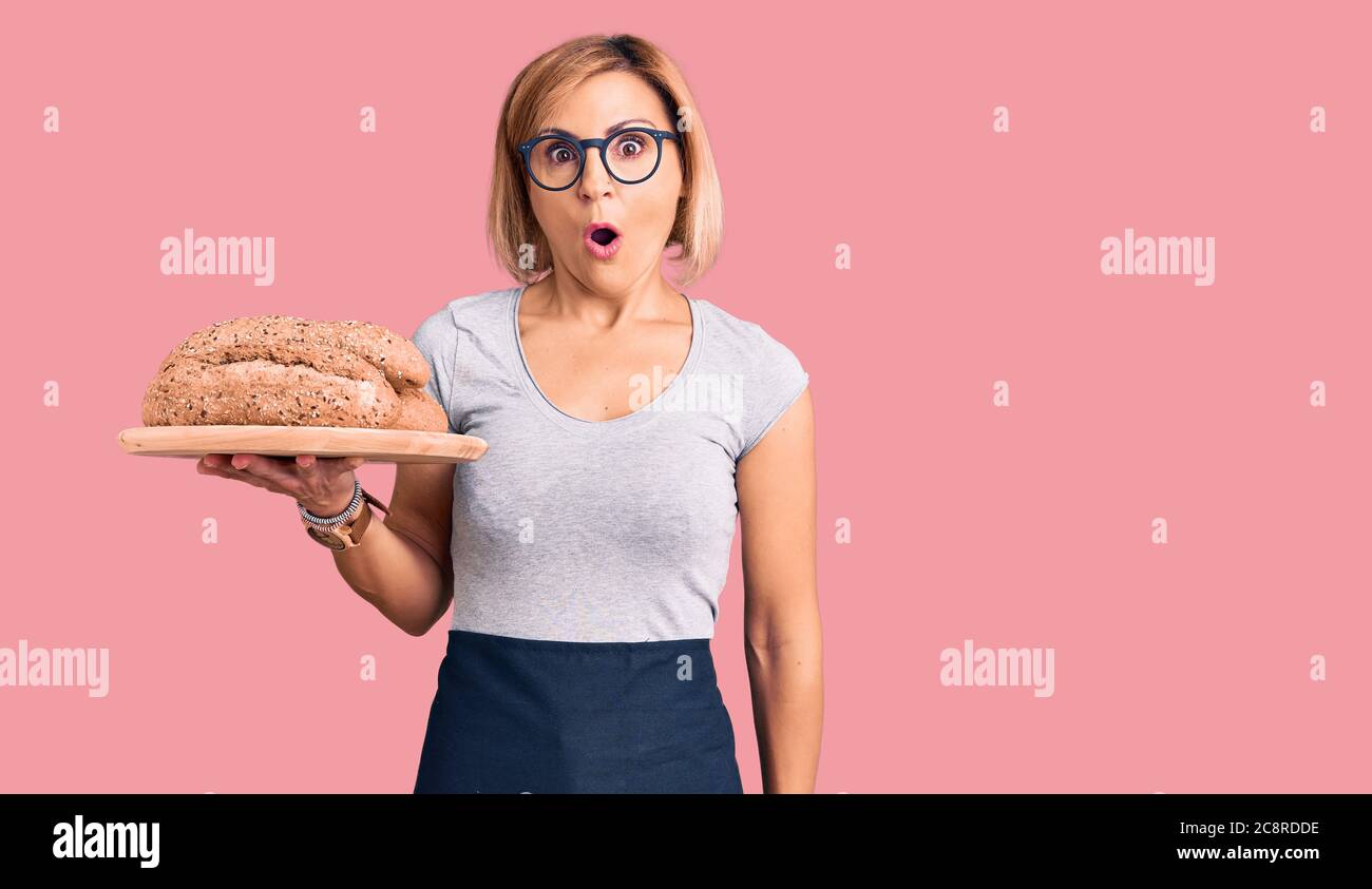 Young blonde woman holding wholemeal bread scared and amazed with open ...