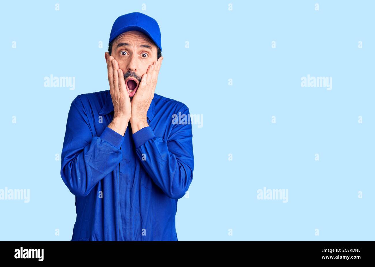 Middle age handsome man wearing mechanic uniform afraid and shocked ...