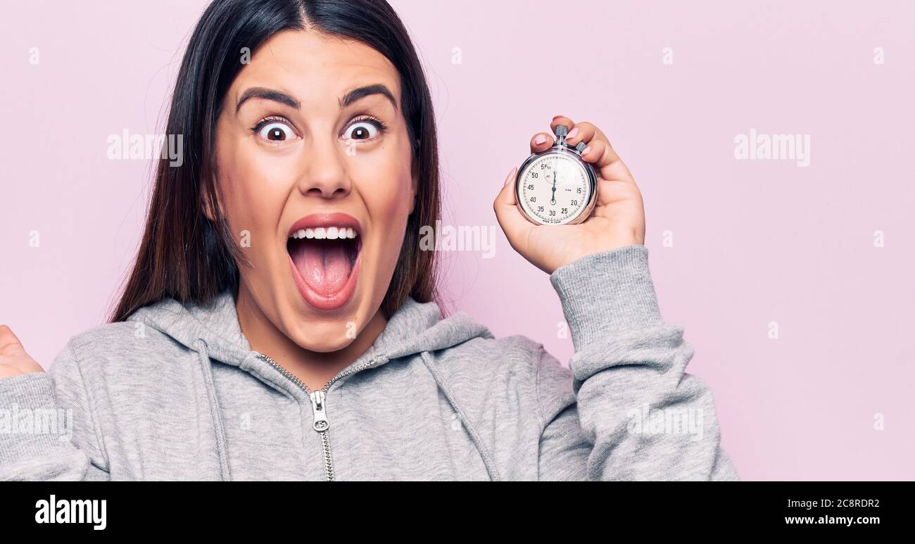 Young beautiful brunette sporty woman holding stopwatch over isolated ...