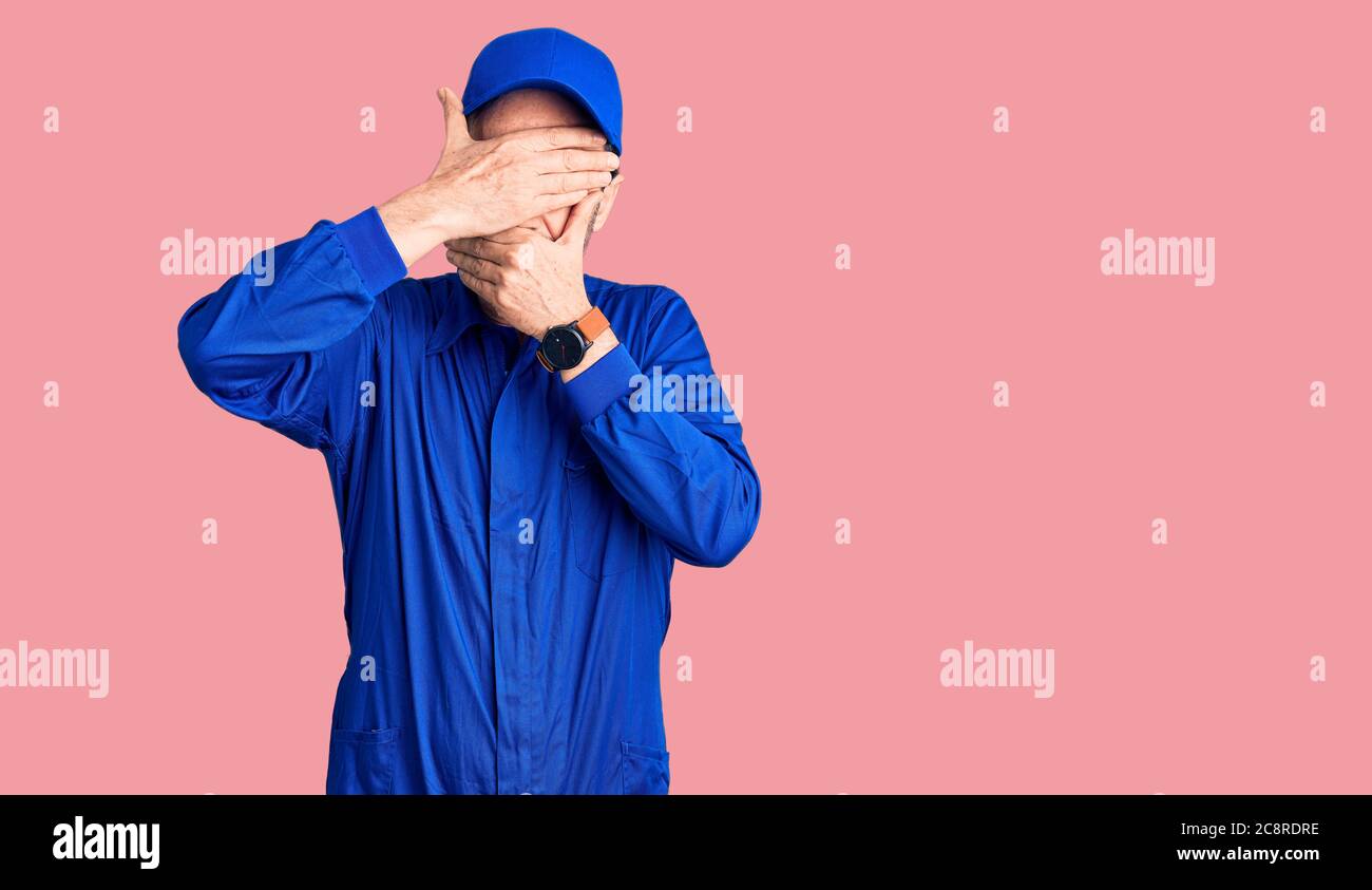 Middle age handsome man wearing mechanic uniform covering eyes and ...