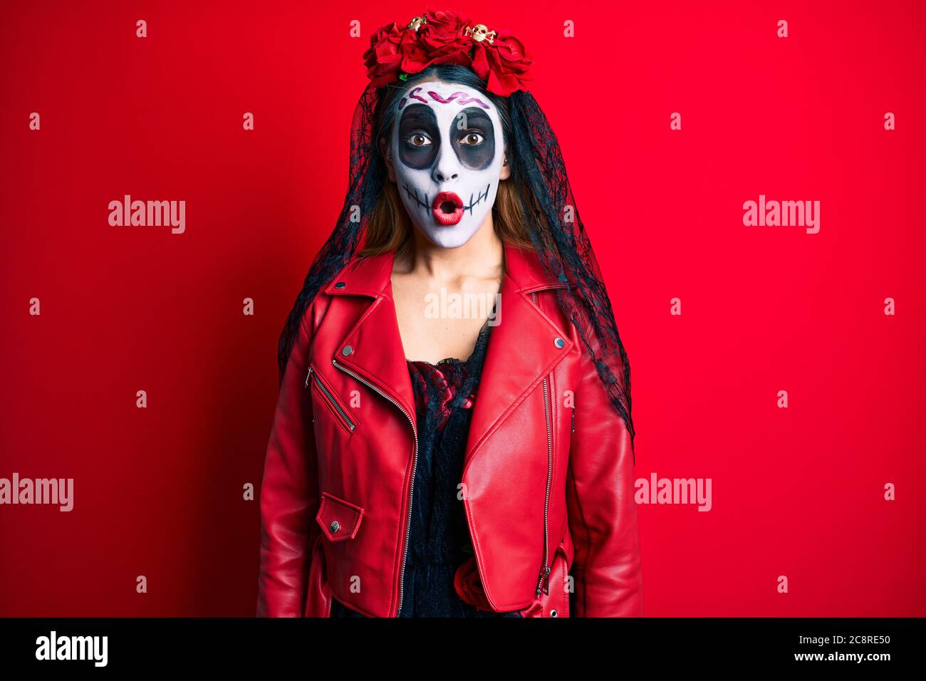 Woman wearing day of the dead costume over red afraid and shocked with ...