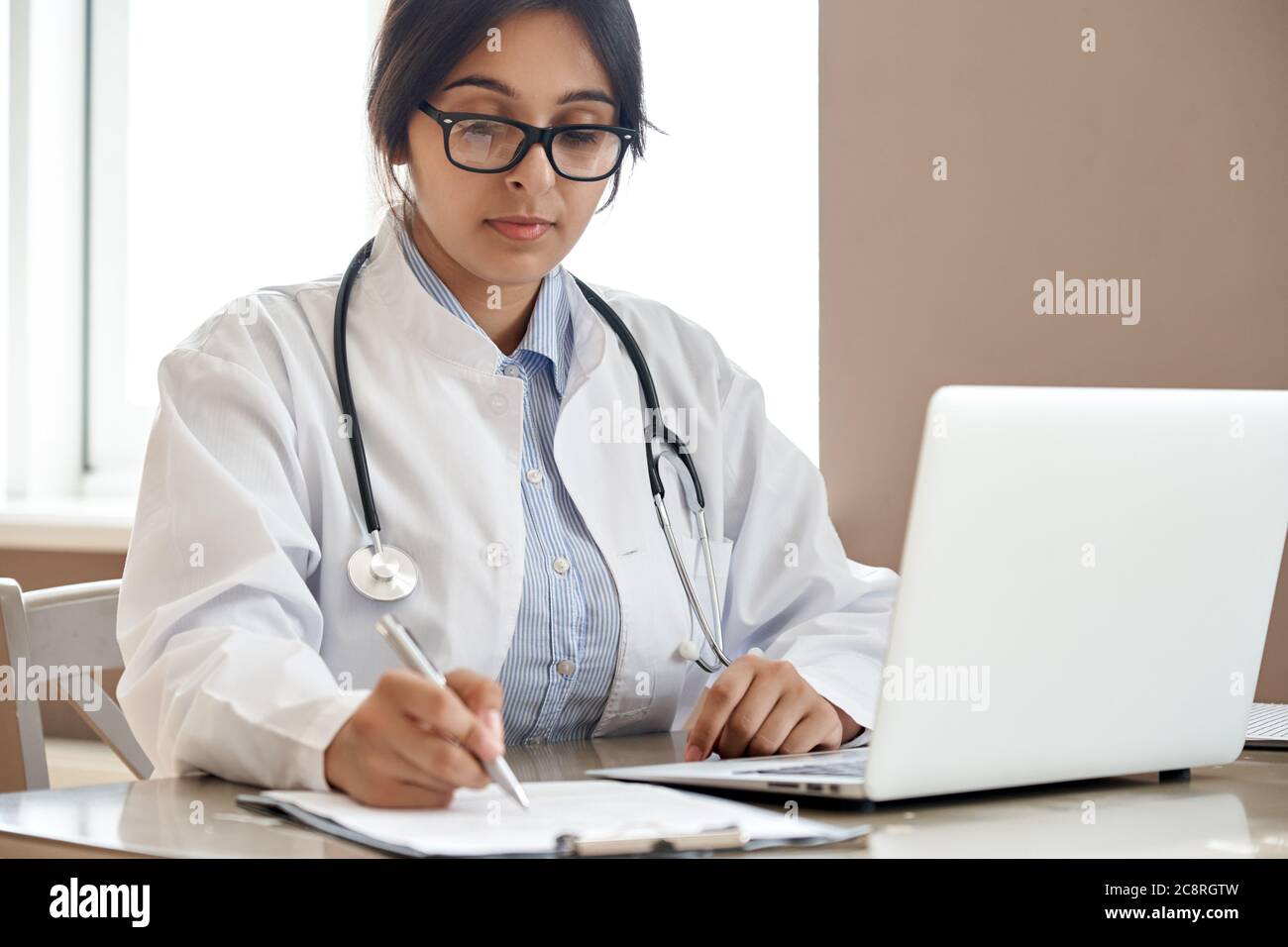 Indian female doctor filling medical form working with laptop at ...