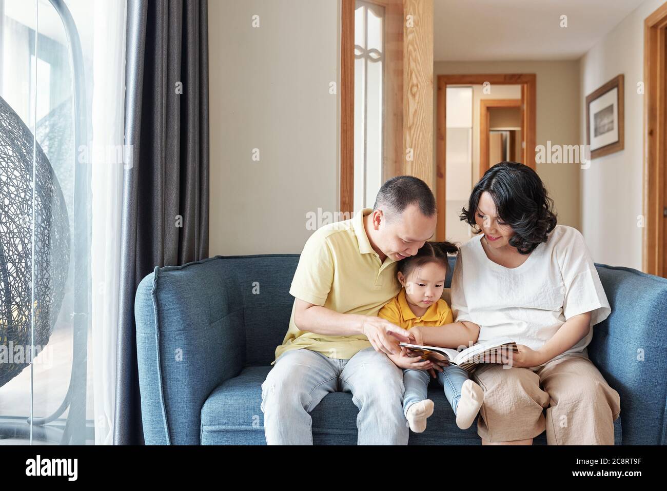 Happy Vietnamese father and mother sitting on sofa and reading ...