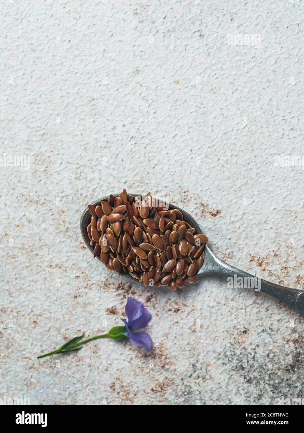 Flax seeds and flaxseed flower. Brown linen seeds in spoon on old white and gray textured ...
