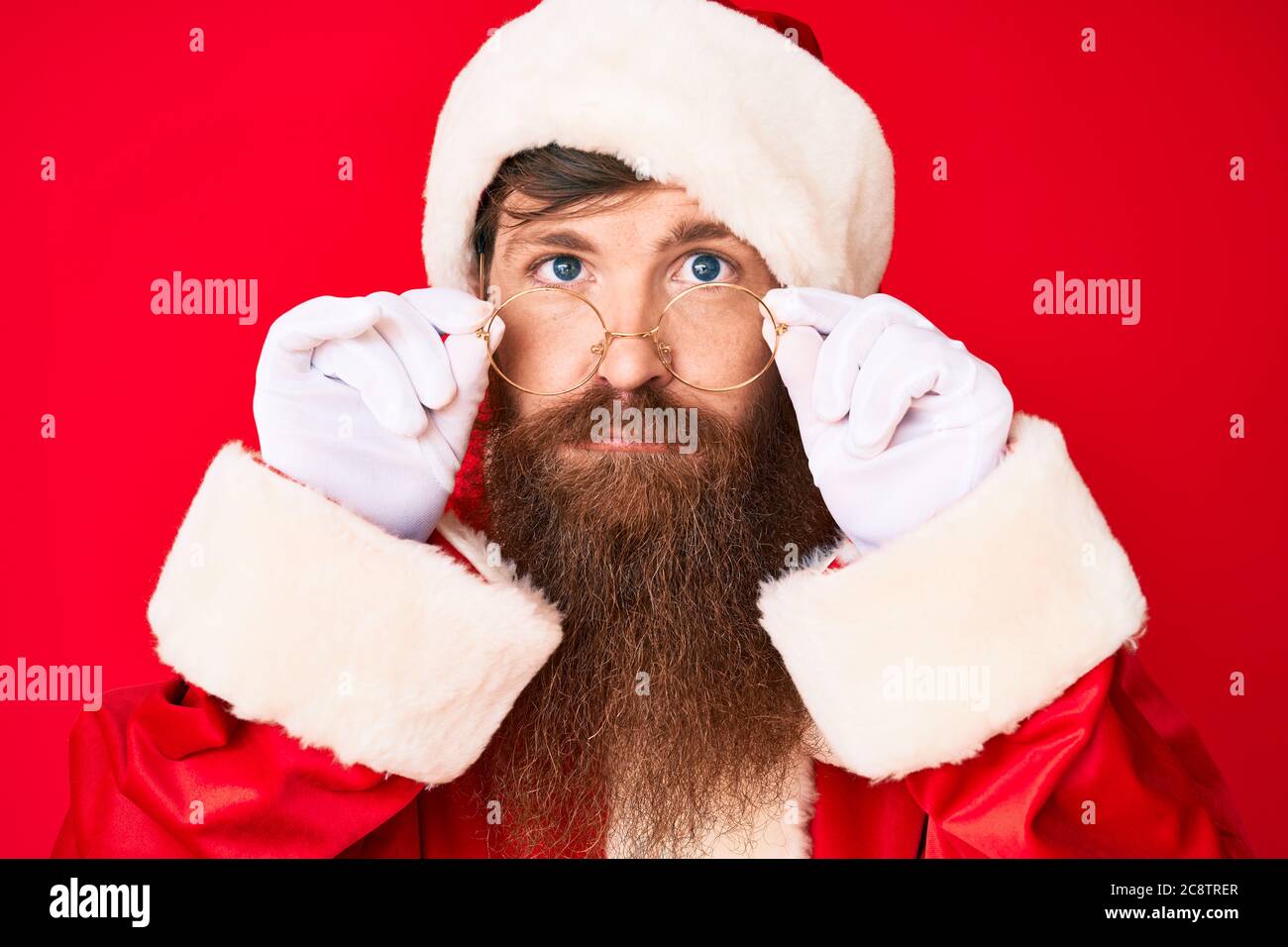 Handsome young red head man with long beard wearing santa claus costume ...