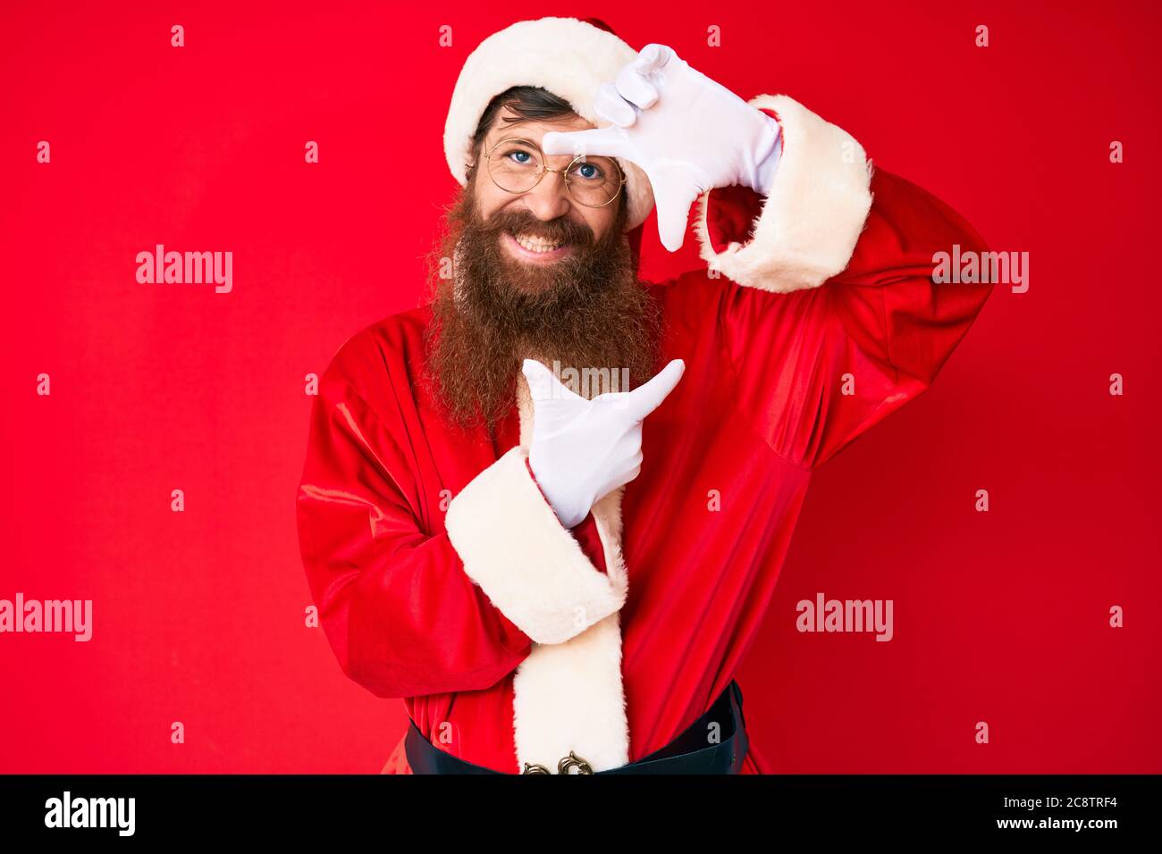 Handsome young red head man with long beard wearing santa claus costume ...