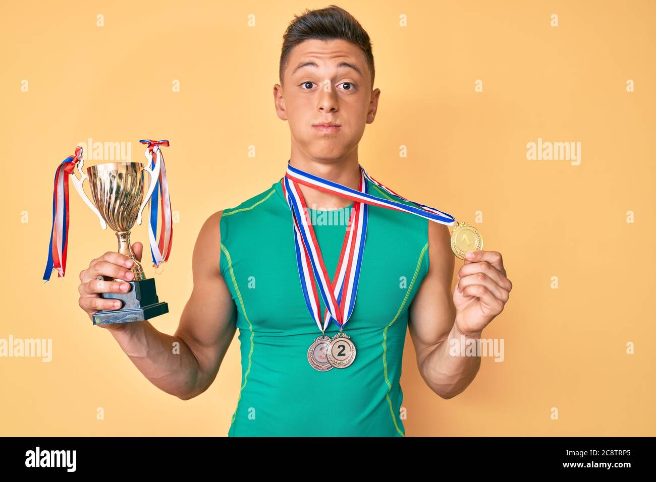 Young hispanic boy holding champion trophy wearing medals puffing ...