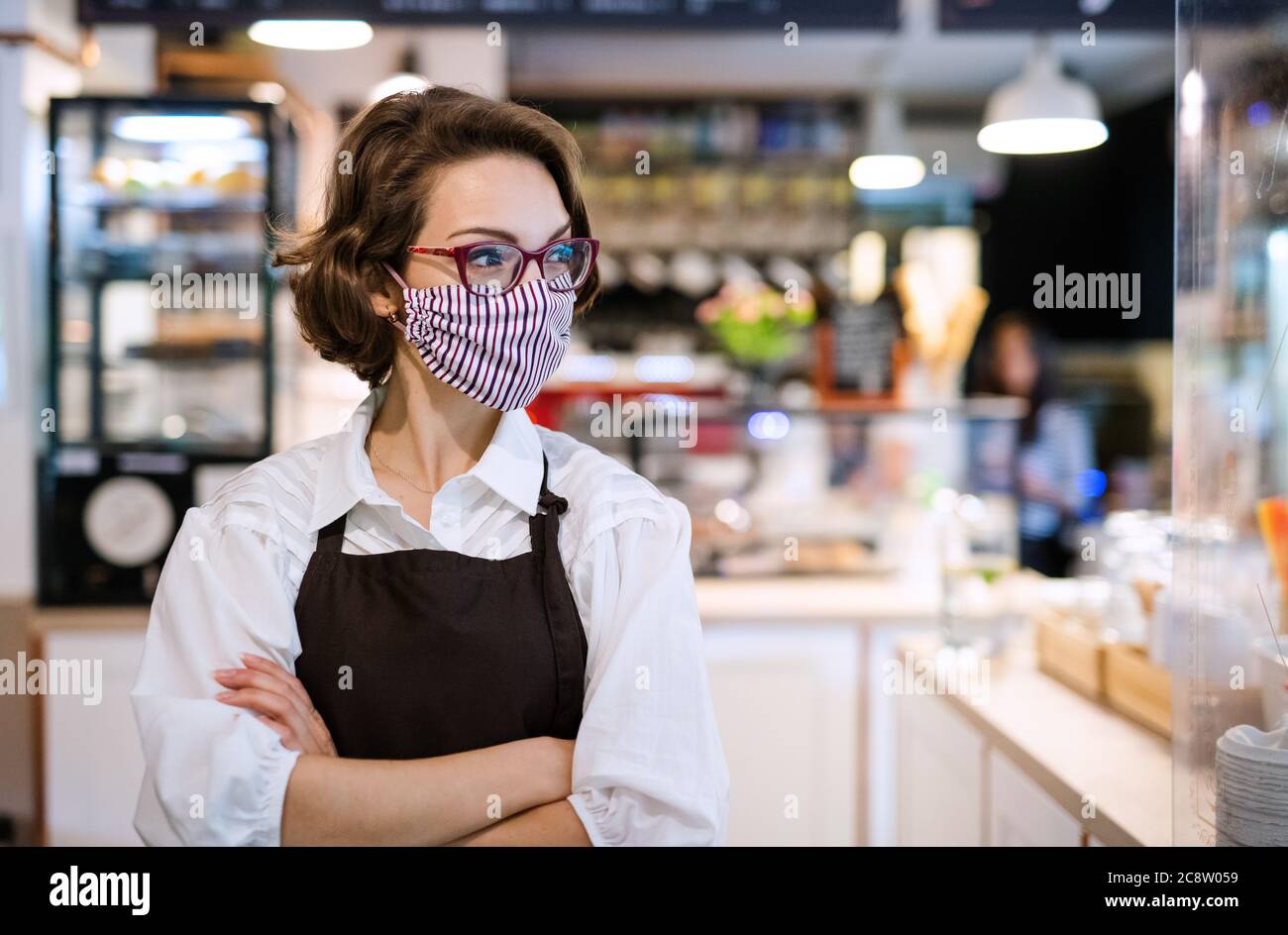 Young waitress with face mask standing in cafe, arms crossed Stock ...