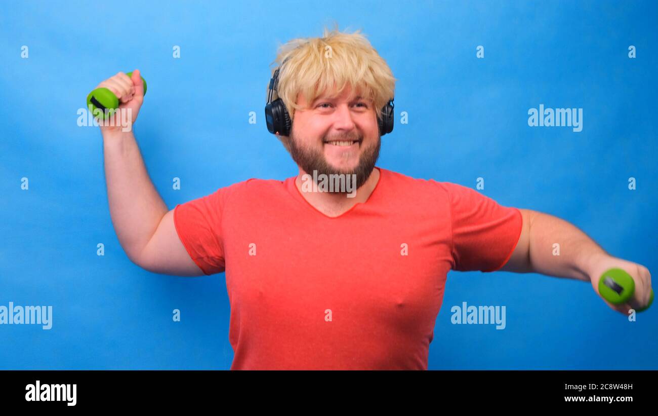 Funny fat man freaky in a wig and a pink t-shirt with dumbbells doing ...
