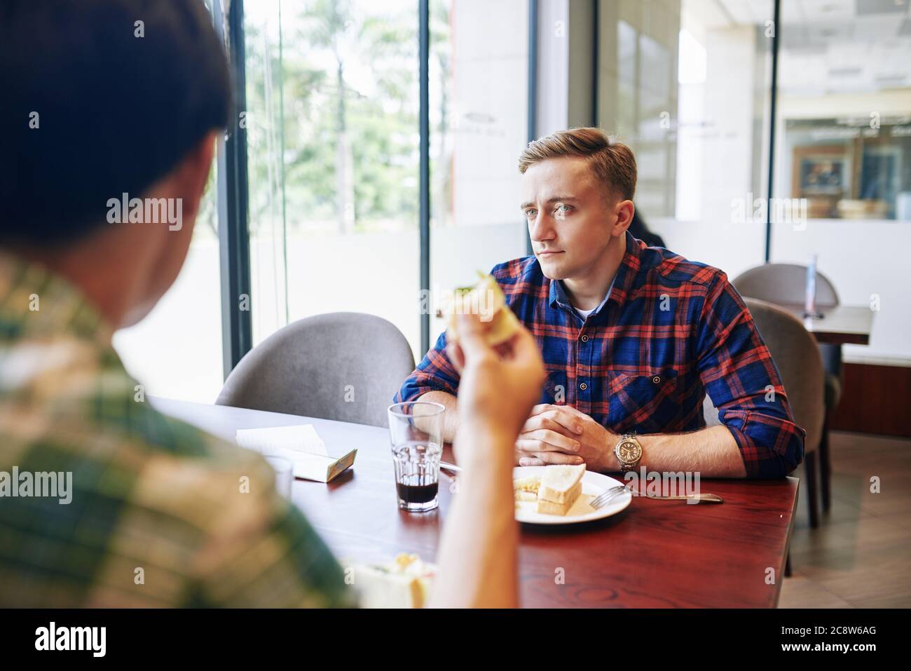 Serious handsome young man and plaid shirt sitting at cafe table and ...