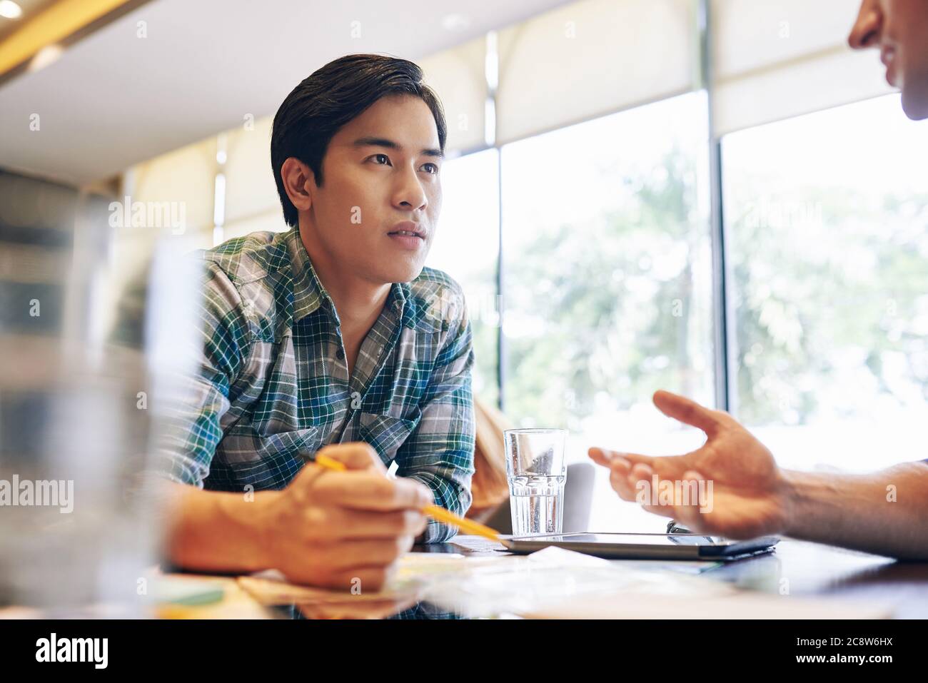 Serious young Vietnamese man putting on document on cafe tablet when ...