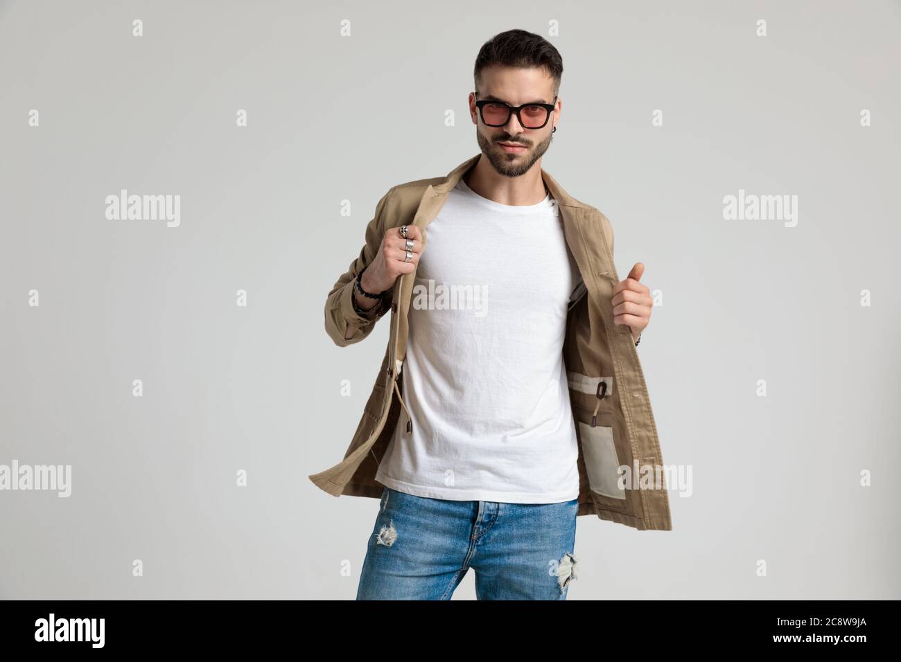 happy young man wearing sunglasses, fixing and opening jacket, smiling ...