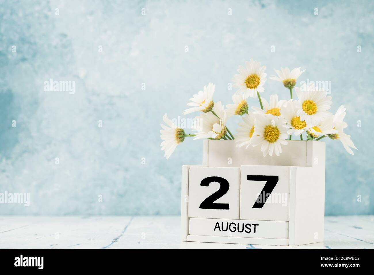 White cube calendar for august decorated with daisy flowers over blue ...