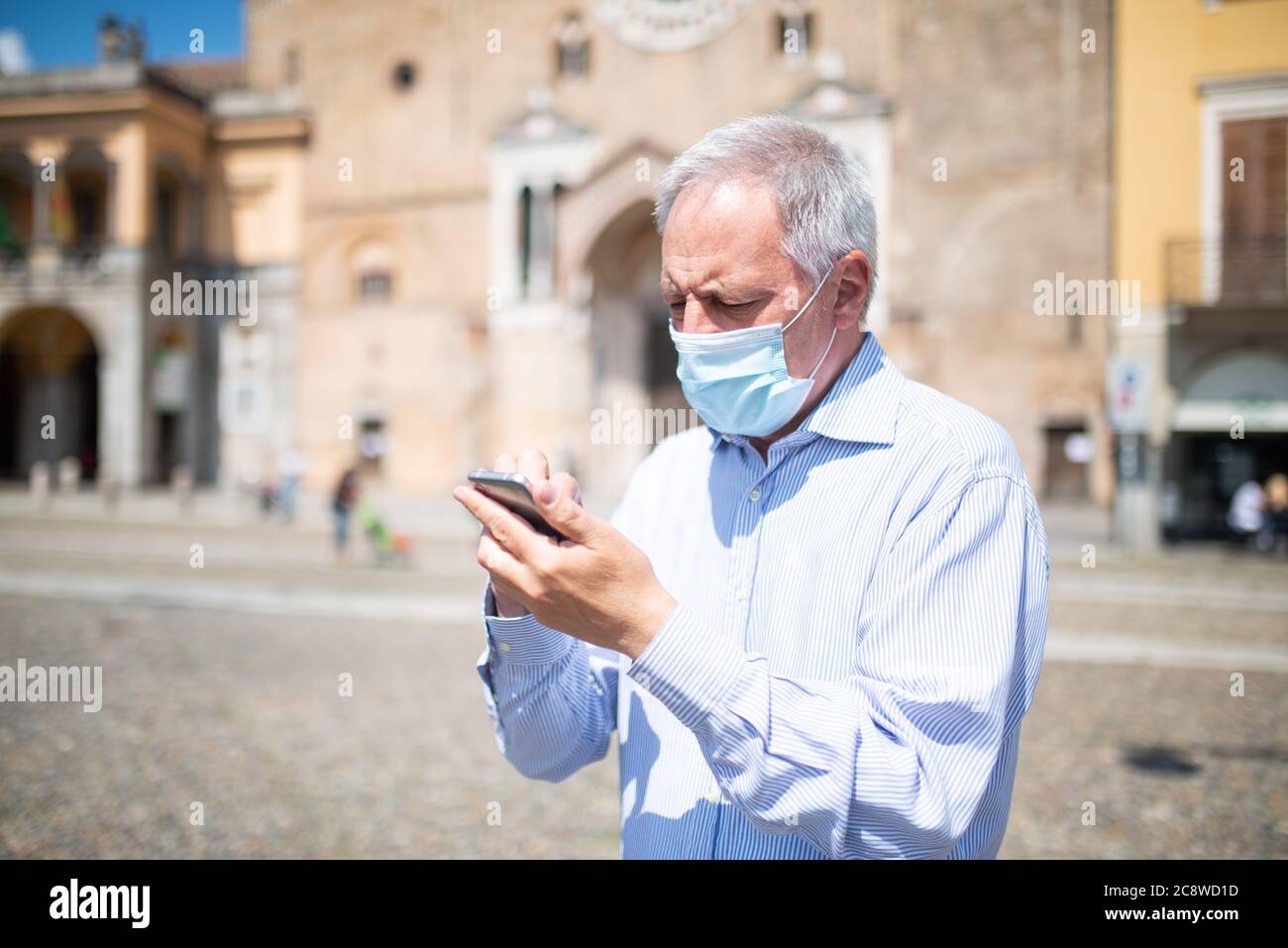 Masked man using his smartphone outdoor in a big european square Stock ...