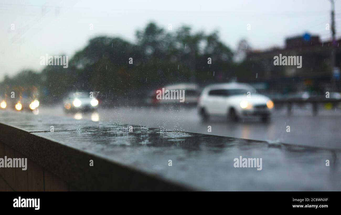 Urban rainy landscape. Drops on parapet along a busy road with cars ...
