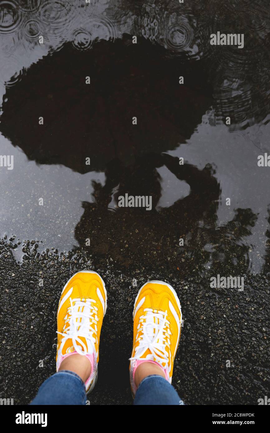 Reflection of person with umbrella in puddle and yellow sneakers Stock ...