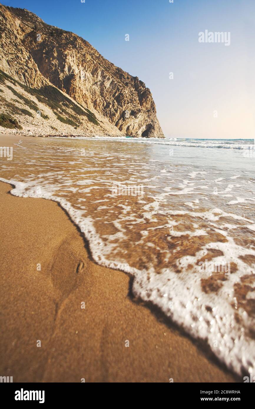 Vertical shot of ocean water receding from the sandy shore with a rock ...