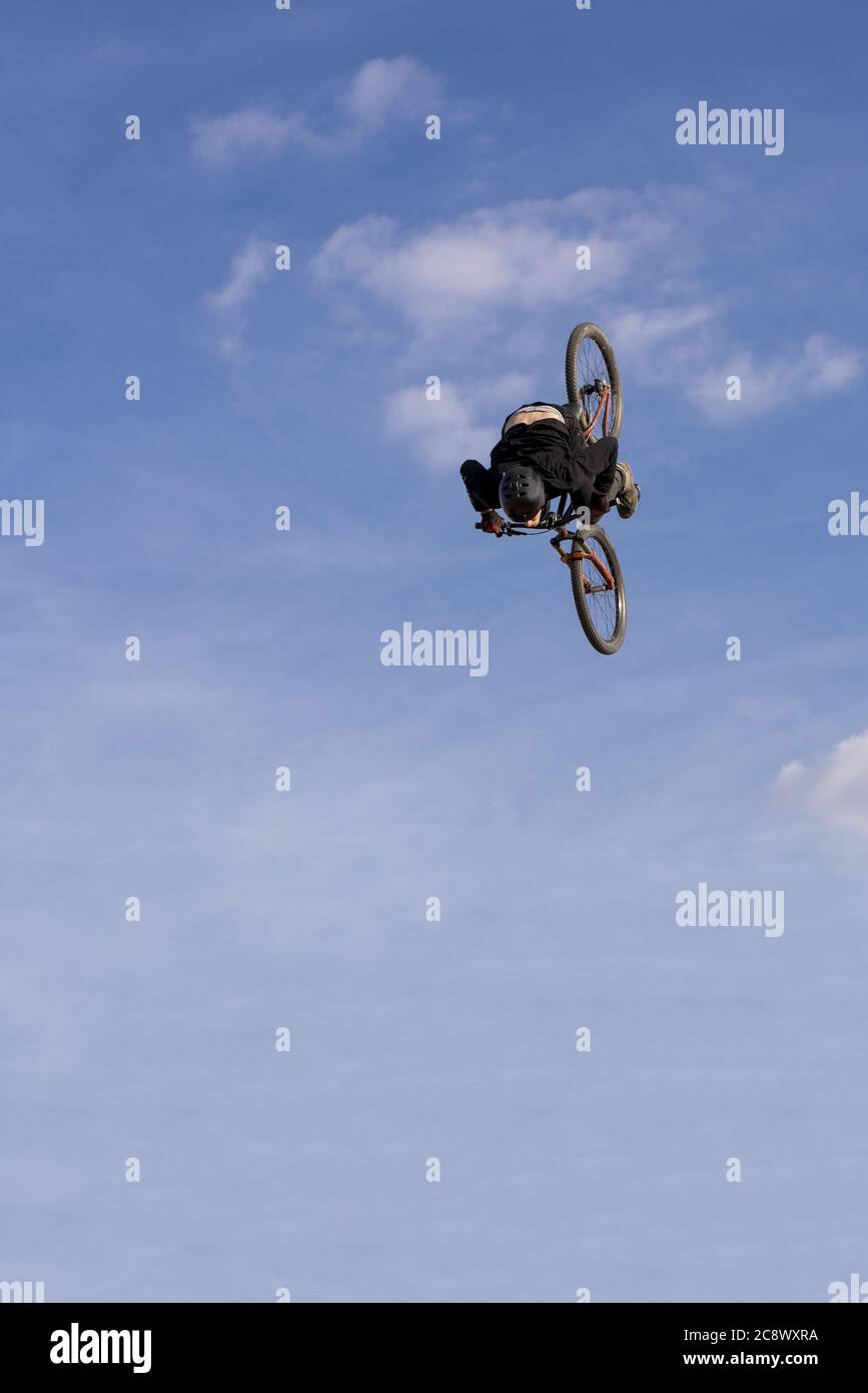 Vertical shot of a biker flying on blue sky and white clouds background ...