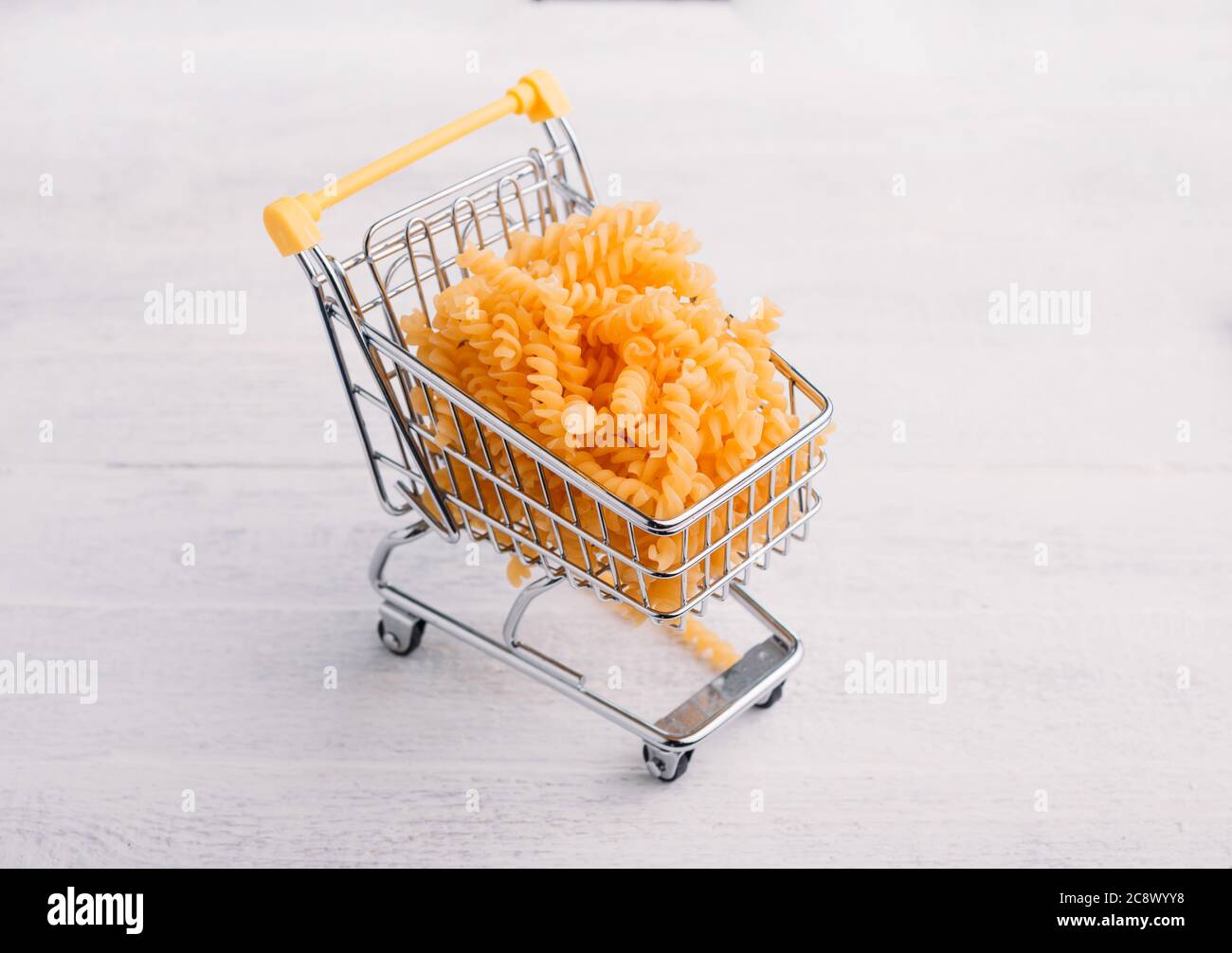 Close up photo of small shopping trolley with pasta over white wooden ...