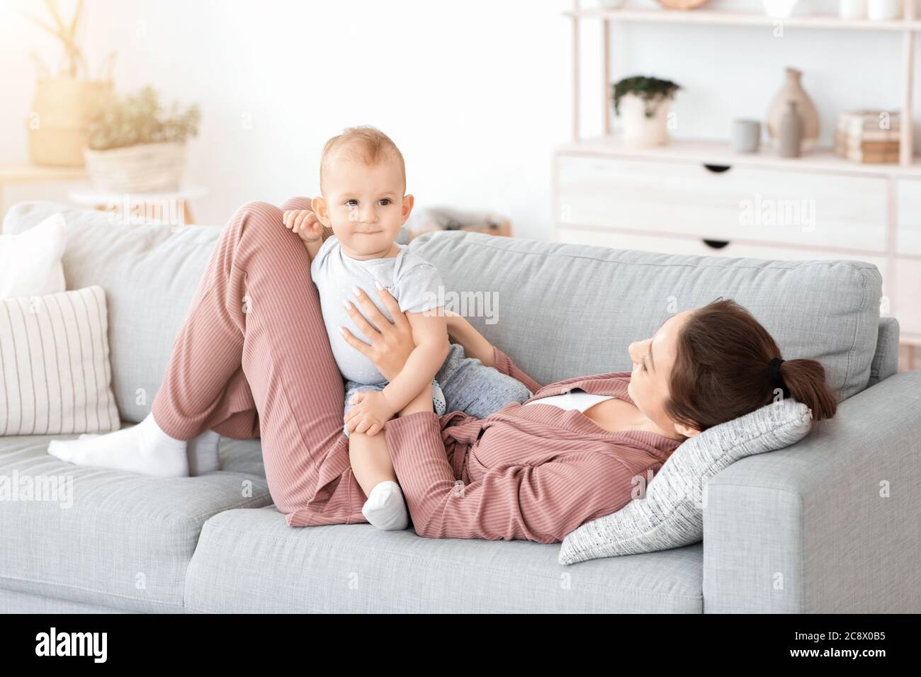 Adorable baby boy and young mom relaxing together on couch at home ...