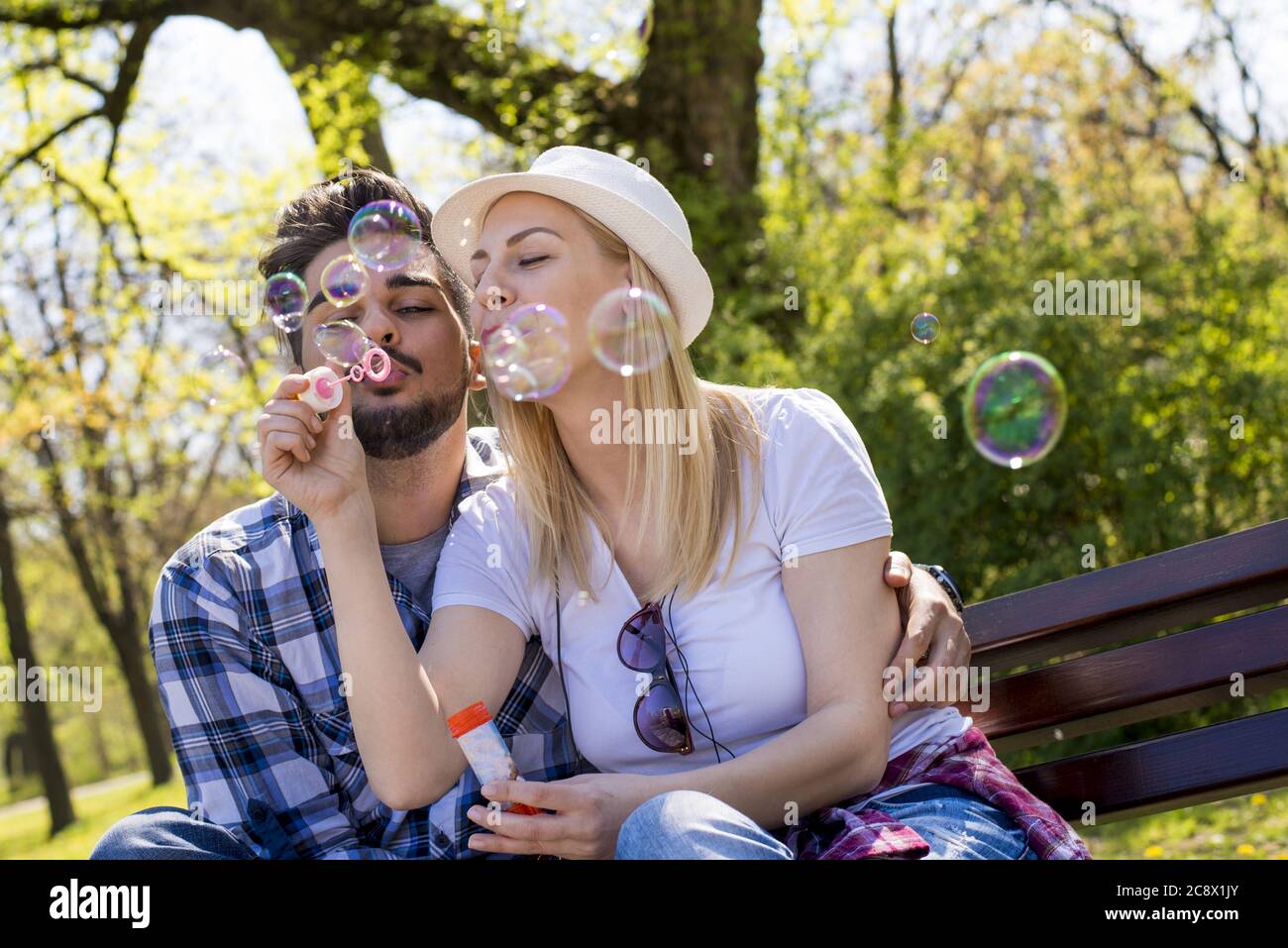 Young attractive couple having fun while blowing bubbles together on a park bench Stock Photo ...