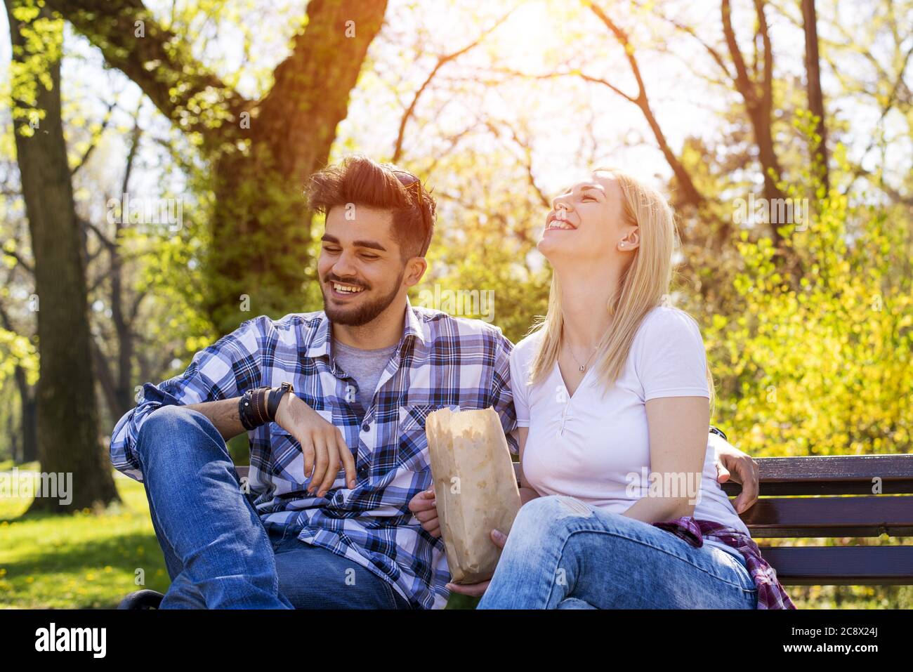Attractive young couple having fun and eating popcorn on a park bench ...