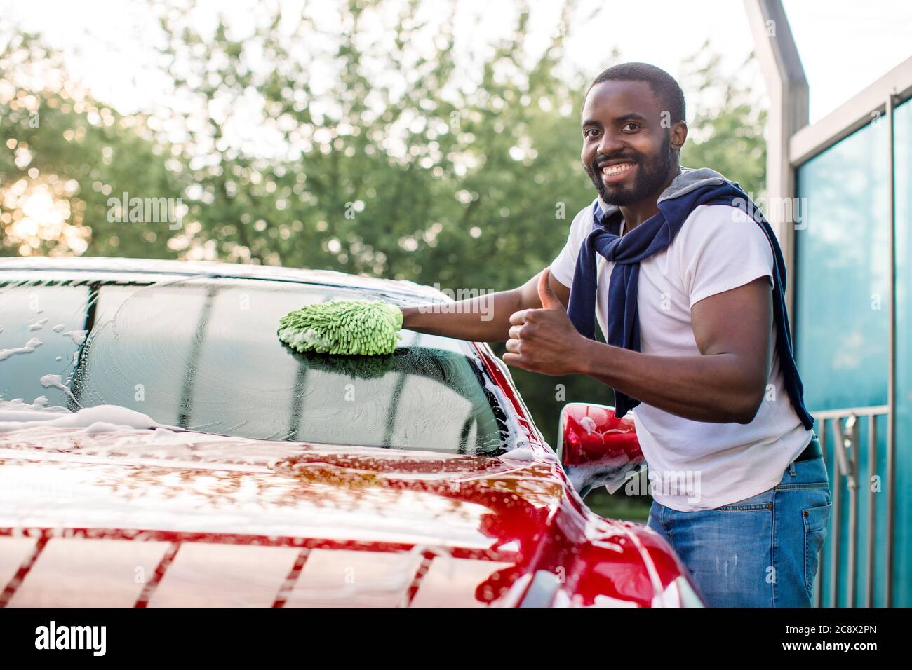 Outdoor car wash with sponge and foam. Car washing. Smiling African man ...