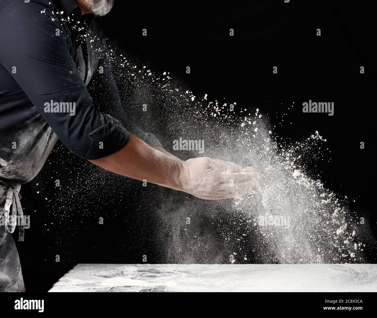 chef in black uniform sprinkles white wheat flour in different ...