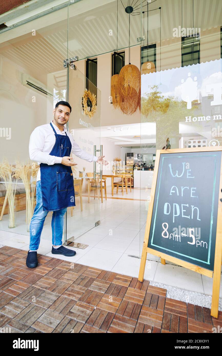 Smiling handsome bakery owner making welcoming gesture and inviting ...