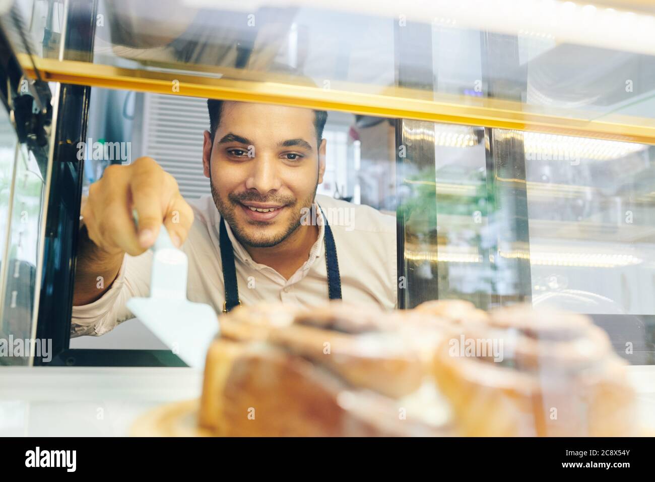 Positive waiter taking cinnamon bun from showcase for customer Stock ...