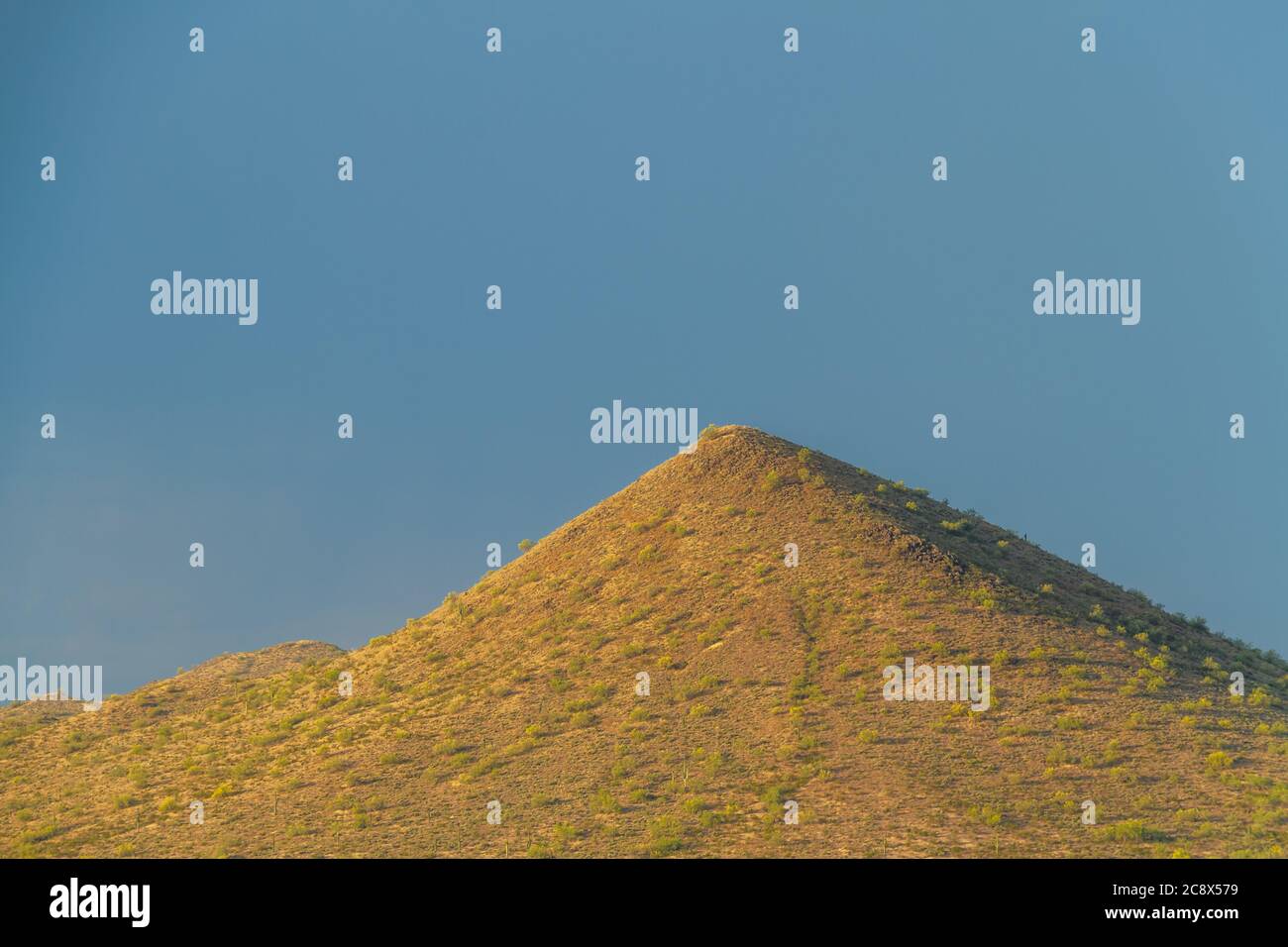 A desert mountain lit by the morning sun with dark, ominous clouds in ...