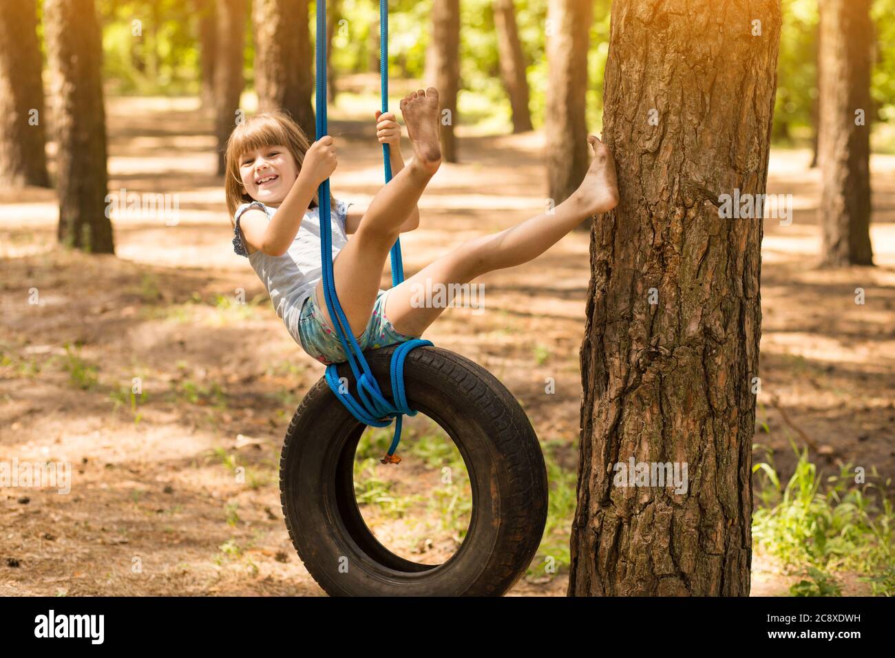Happy active child girl playing on swing wheel in forest on sunny ...