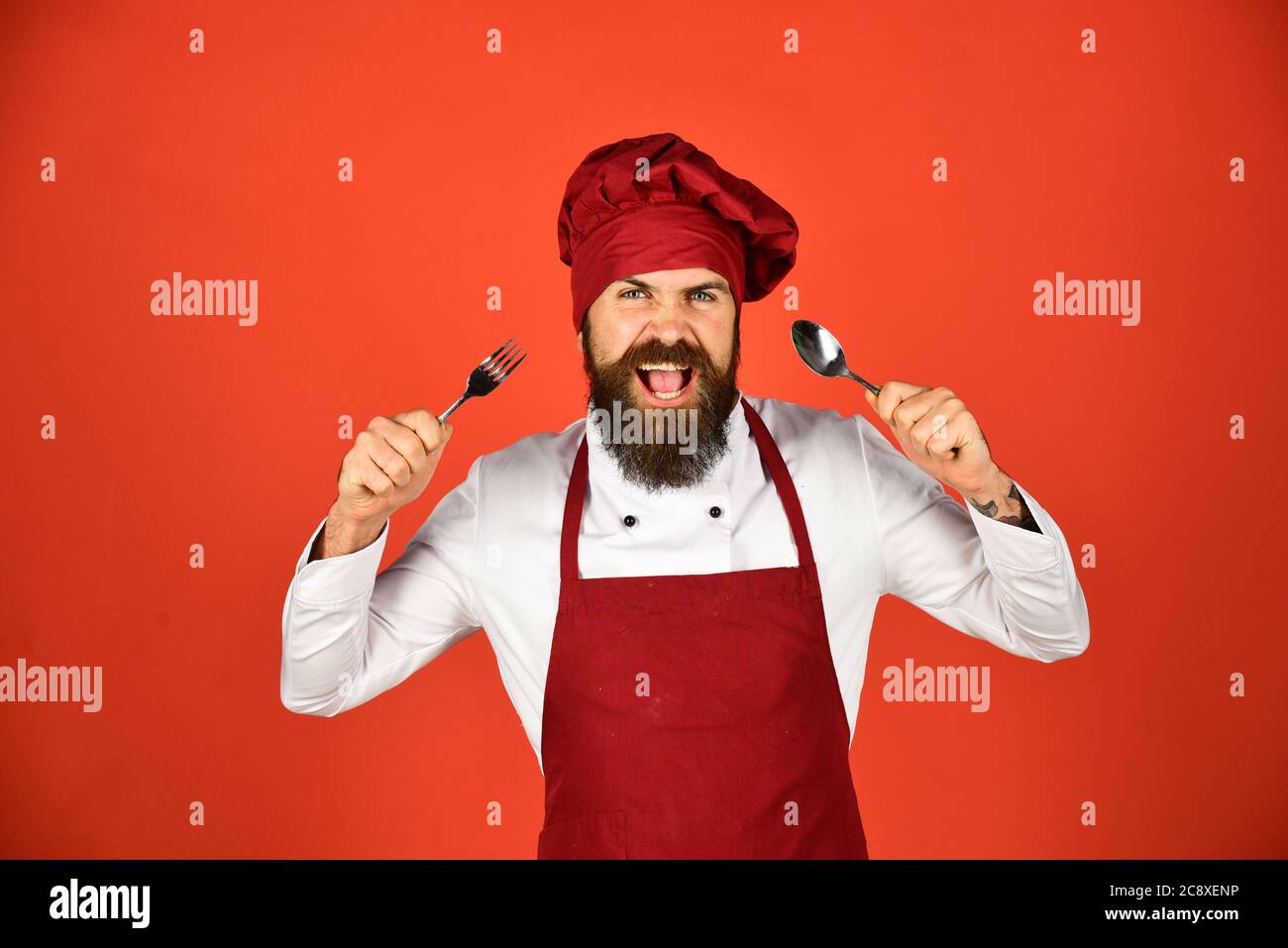 Man with beard holds kitchenware on red background. Chef holds cutlery ...