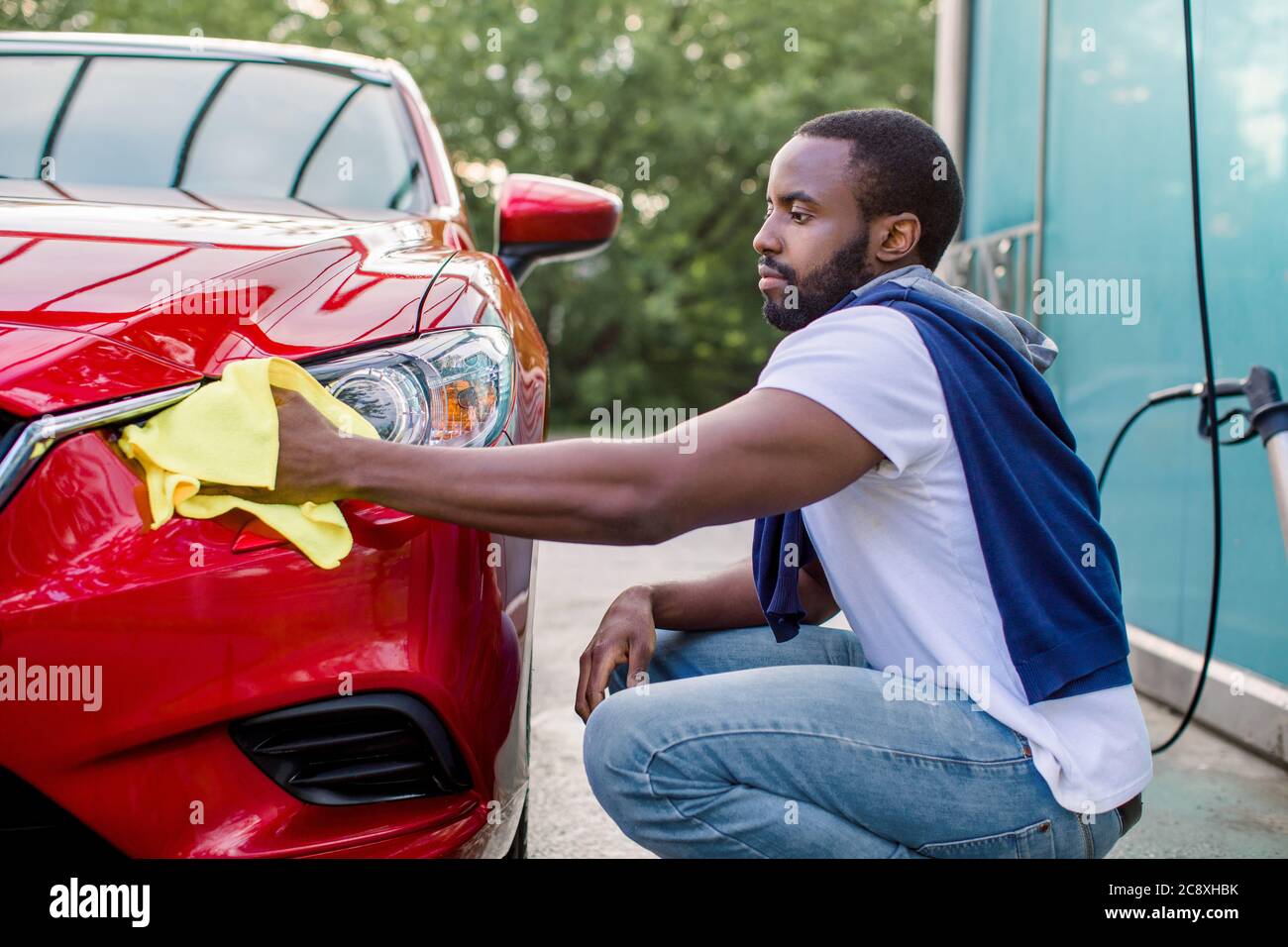 Young African man washing and wiping his red car headlight at the ...