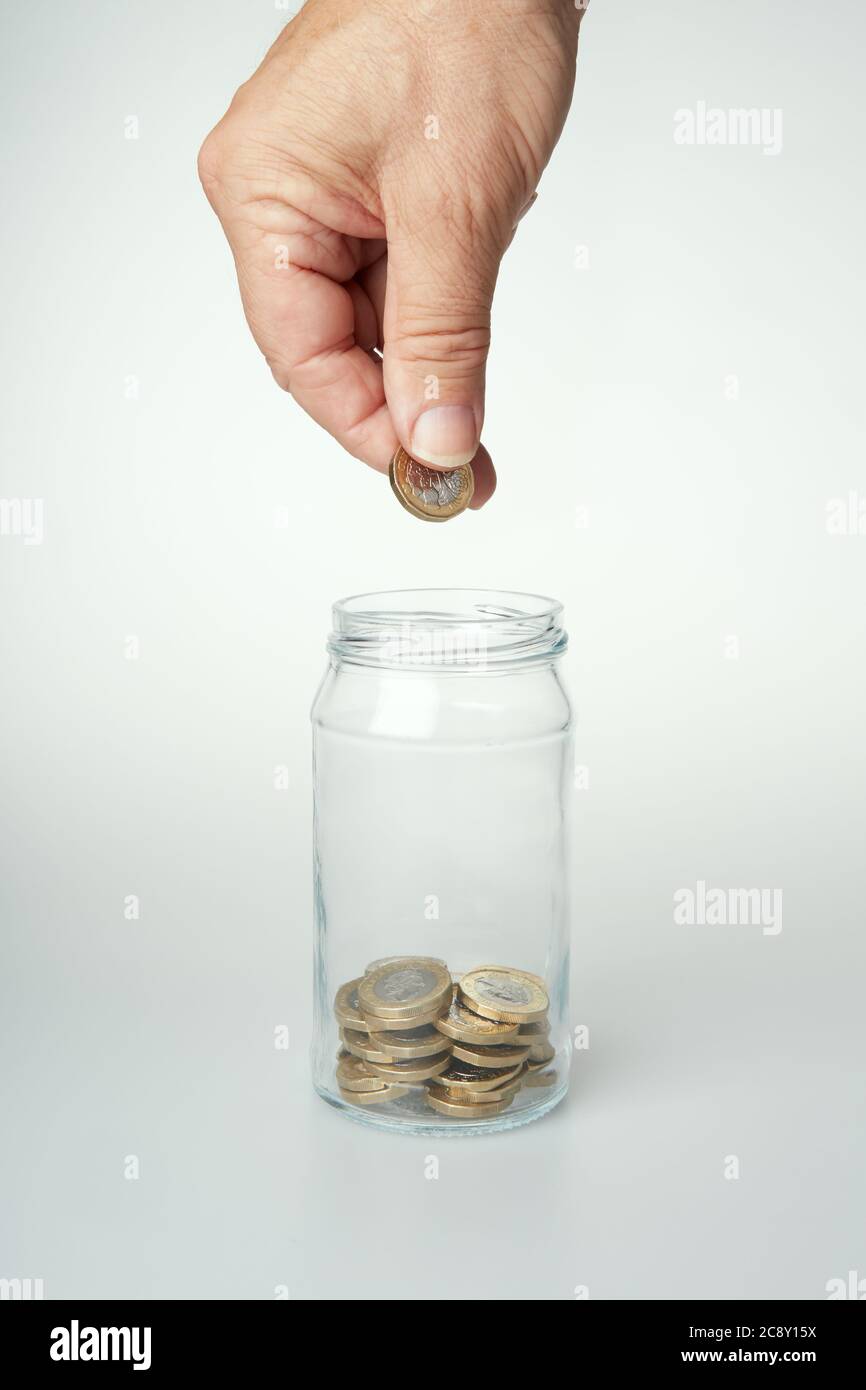 Photograph of a man's hand holding a £1 coin ready to drop into a glass ...