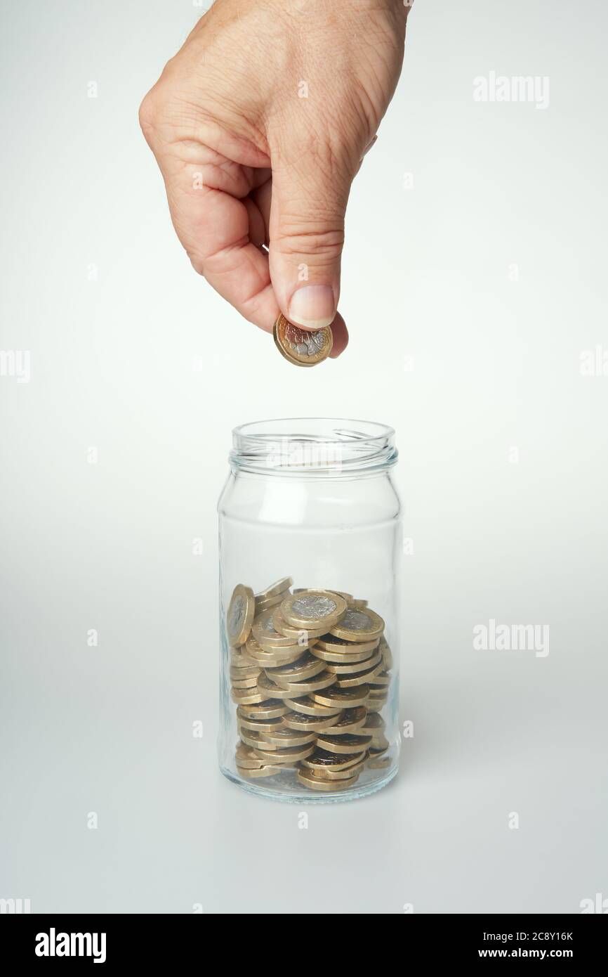 Photograph of a man's hand holding a £1 coin ready to drop into a glass ...