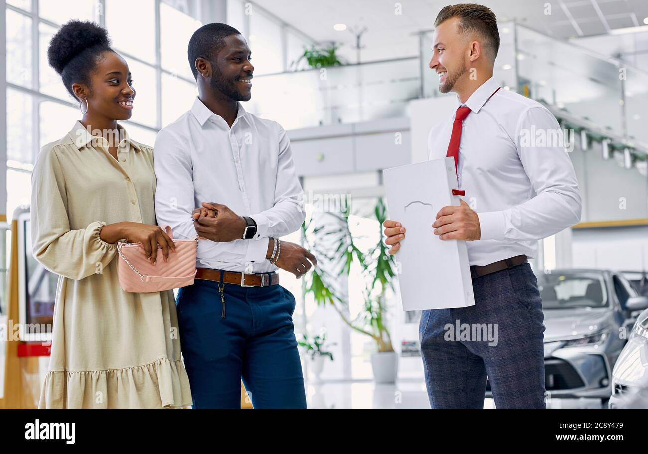 handsome young car salesman telling about the features of the car to ...