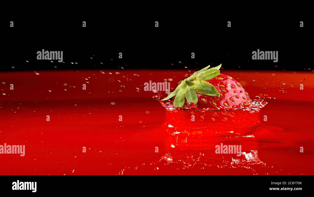 Strawberry falling on clear liquid and producing a spectacular splash ...