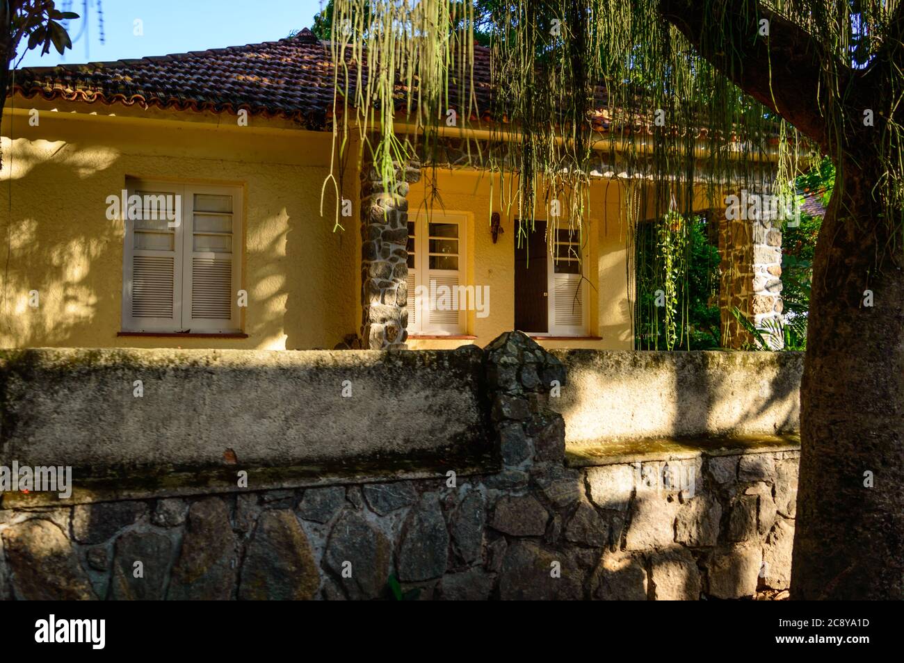 A yellow colonial house with a front porch and big tree in front at ...